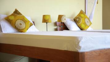 Uma cama com estrutura de madeira, duas almofadas com padrão amarelo e branco, e duas luminárias de cabeceira com abajures amarelos.