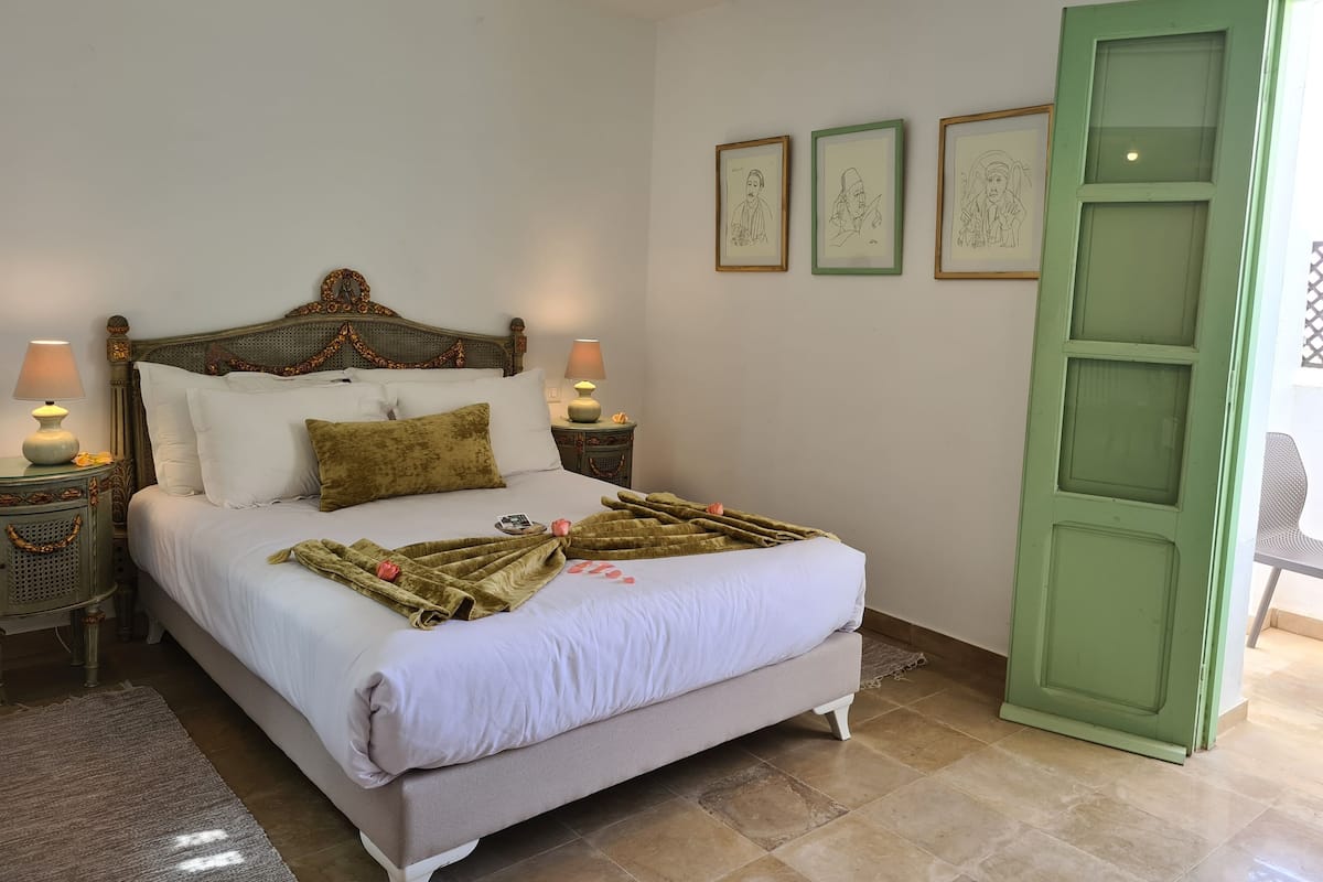 Cama bem arrumada com roupa de cama branca e verde, duas luminárias de cabeceira e uma porta verde.