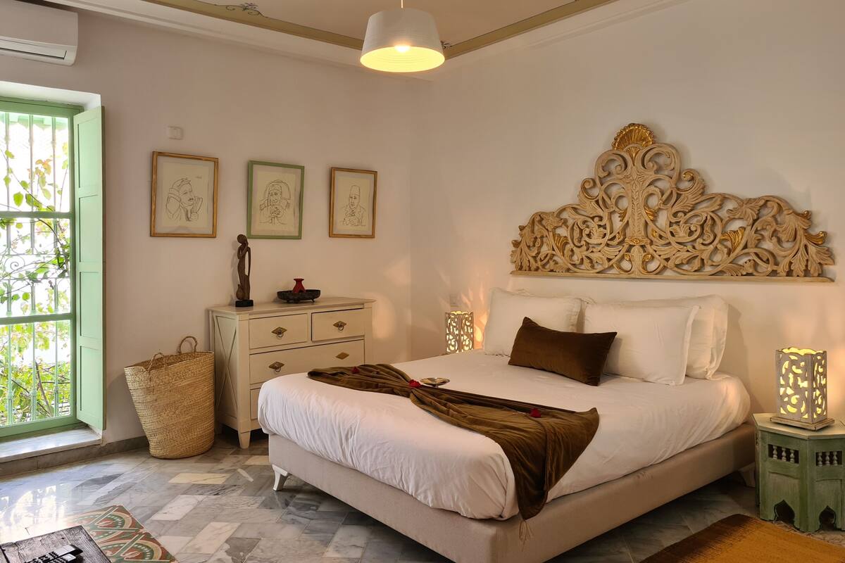 Quarto com cama, cômoda, uma janela grande e obras de arte nas paredes.