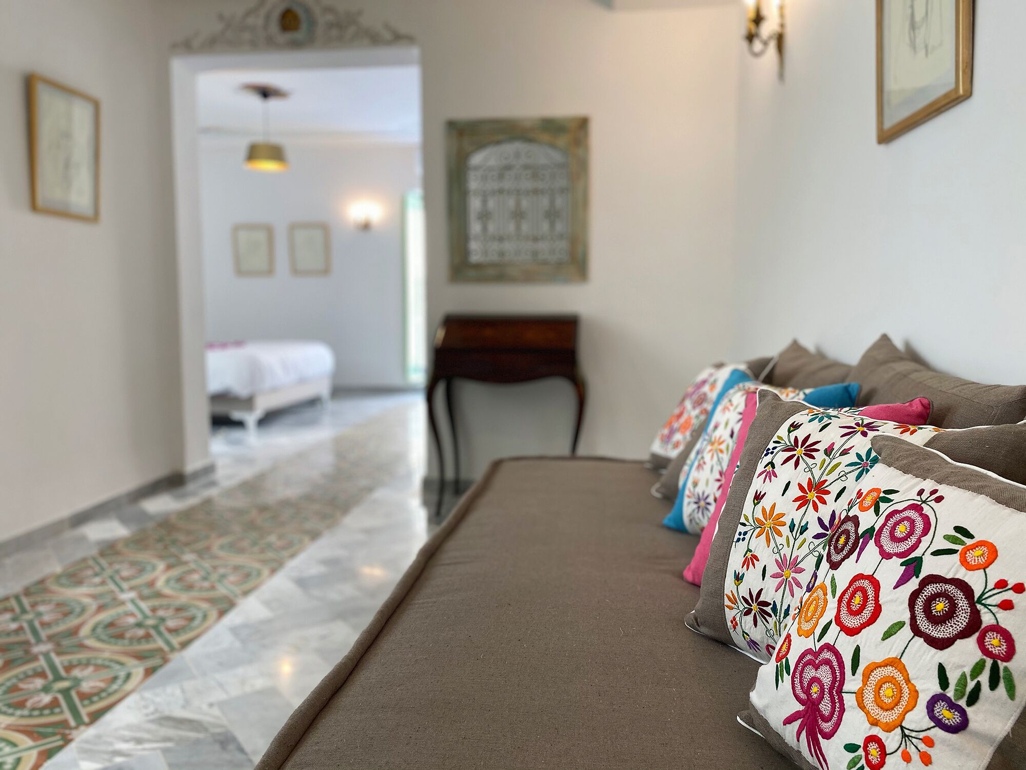 Quarto de hotel com uma cama, um sofá, um tapete estampado e uma parede com obras de arte emolduradas.