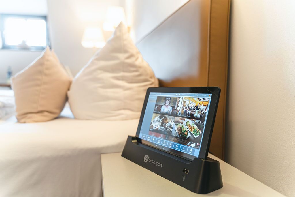 Um tablet exibindo um vídeo apoiado em uma mesa de cabeceira em quarto de hotel.