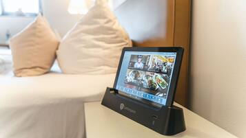 Um tablet exibindo um vídeo apoiado em uma mesa de cabeceira em quarto de hotel.