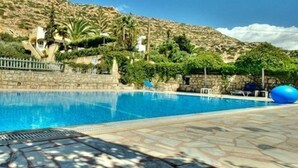 Uma piscina com paredes e deck de pedra, rodeada por vegetação e um cercado branco.