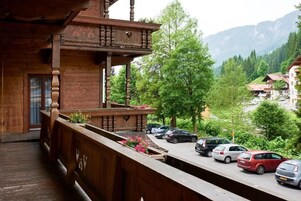 Varanda de madeira com vista para carros estacionados e vegetação ao fundo.