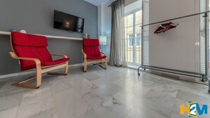 Uma sala de estar moderna com duas poltronas vermelhas, uma televisão de tela plana e uma janela grande com cortinas.