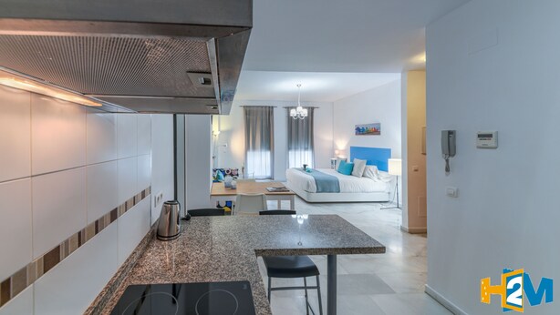 Uma cozinha moderna com fogão embutido, sala de jantar com mesa e cadeiras, e sala de estar com sofá e televisão.