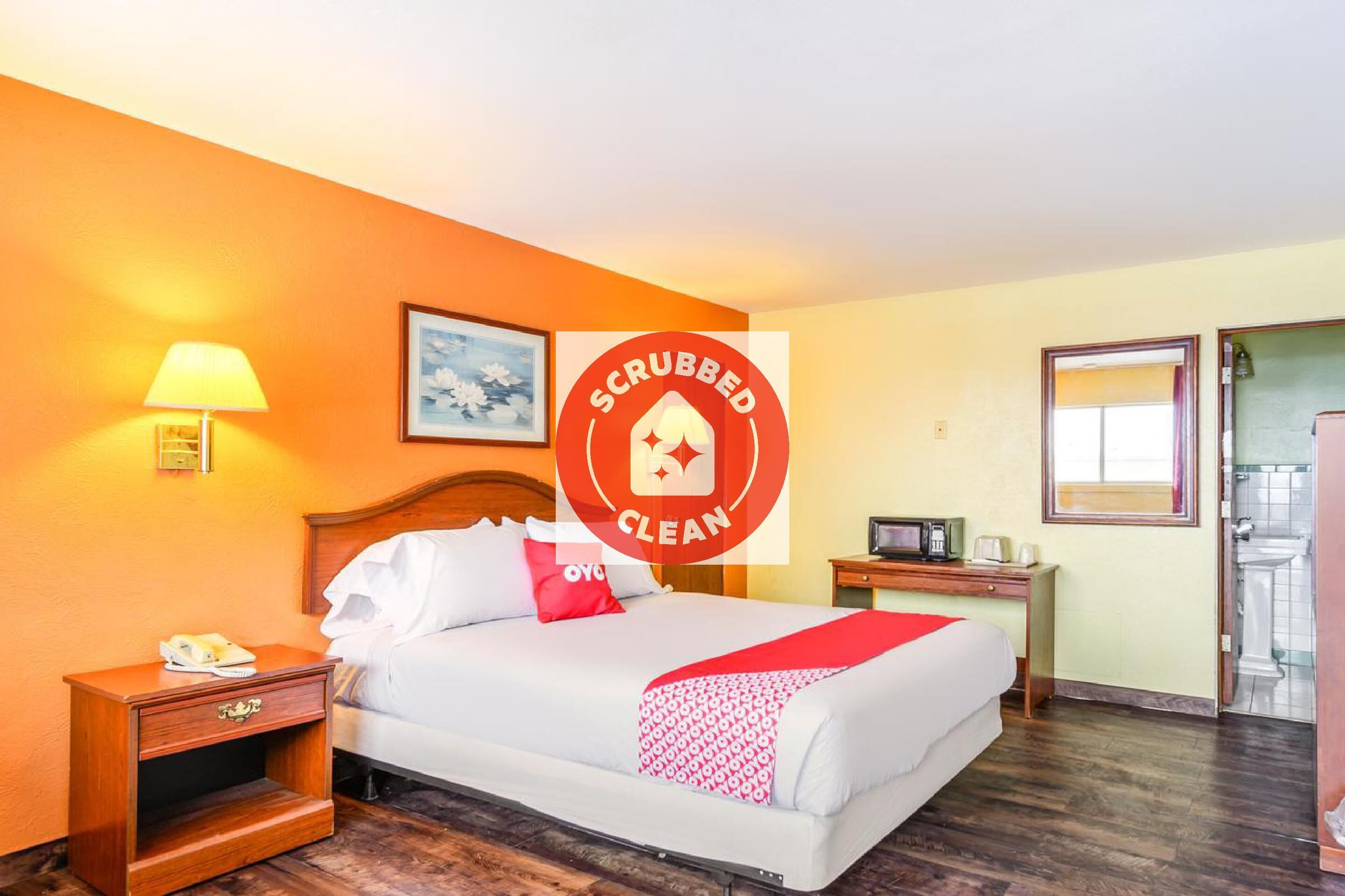 Quarto de hotel limpo com uma cama, mesa de cabeceira, abajur e um quadro na parede.