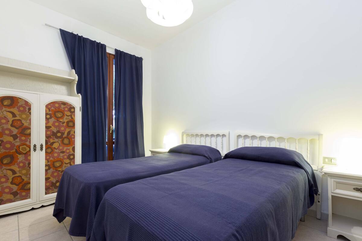 Quarto com duas camas, um guarda-roupa estampado com motivos florais e uma mesa de cabeceira com abajur.