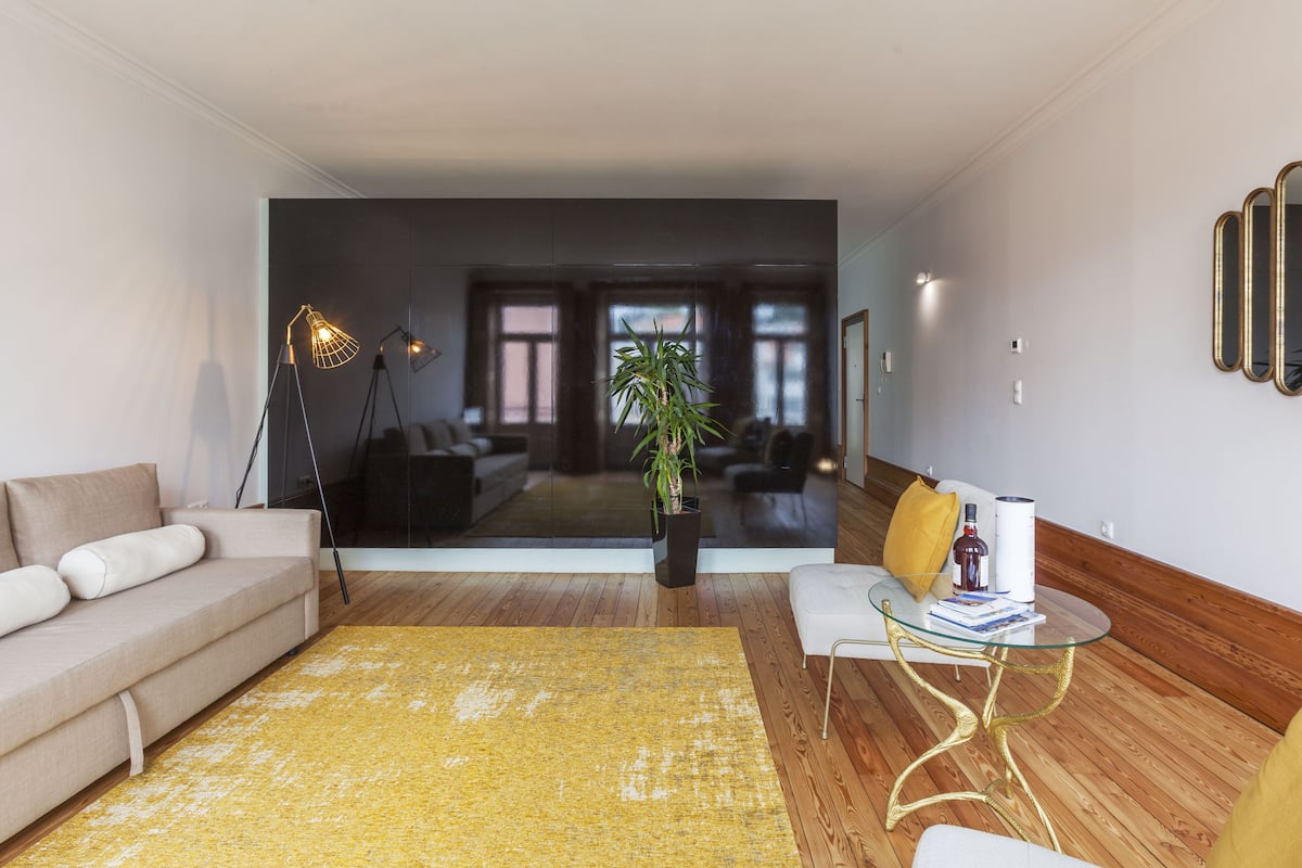 Uma sala de estar moderna com um sofá, uma mesa de centro de vidro, um tapete amarelo e uma planta em vaso.