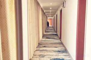 Corredor de hotel com carpete estampado, parede vermelha e porta no final.