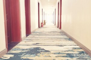 Corredor de hotel com carpete estampado, portas vermelhas e extintor de incêndio.