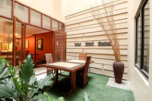 Uma área de refeições com mesa e cadeiras de madeira, divisória de vidro e parede decorativa com linhas horizontais.