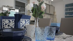 Uma mesa posta com copos de vidro azul, pratos brancos e um vaso com flores.