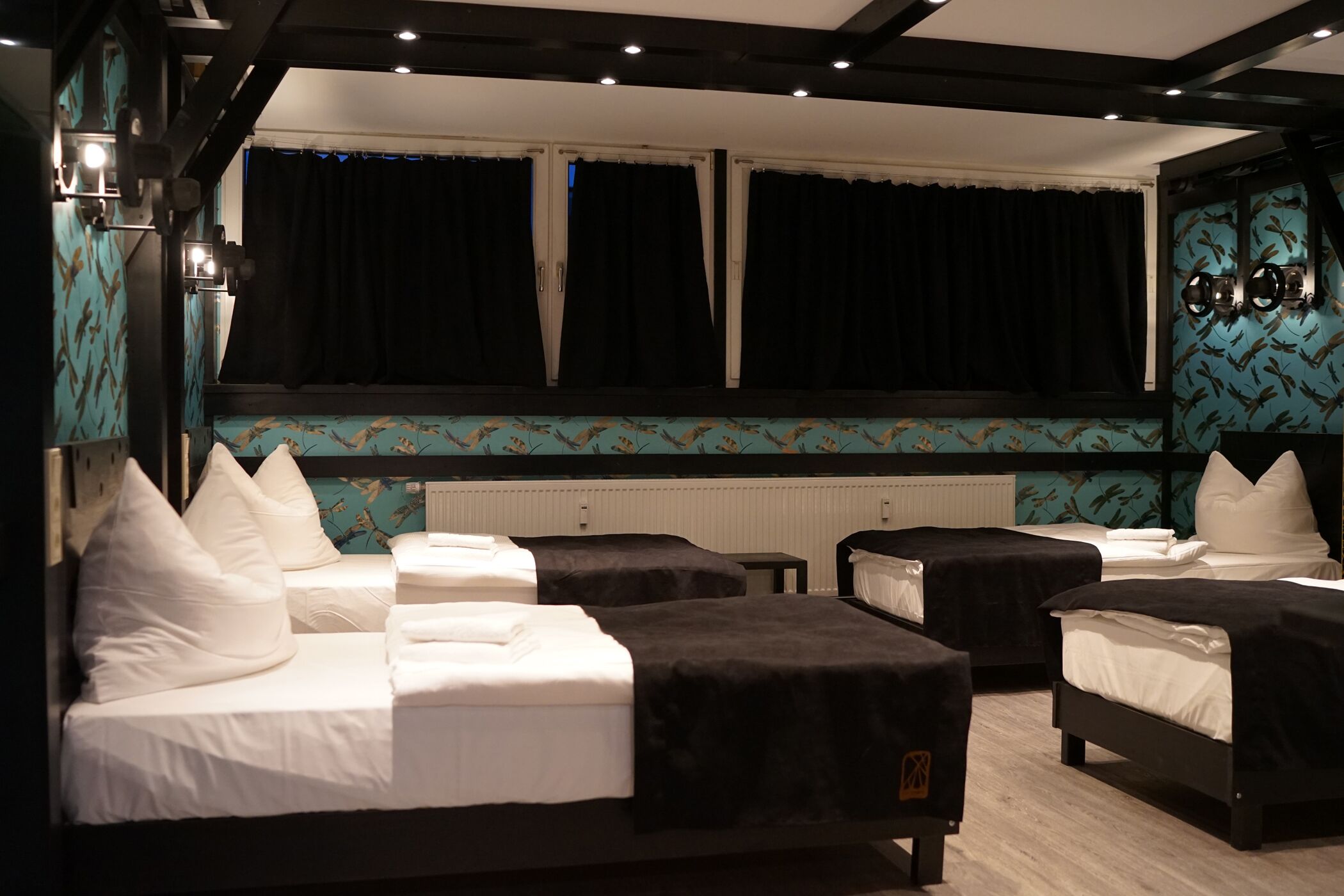 Quarto de hotel com duas camas, uma janela com cortinas e parede estampada.