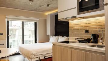 Quarto de hotel compacto com cama, cozinha compacta e vista por uma porta de vidro.