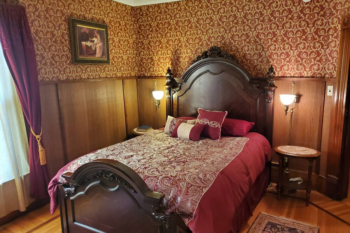 Um quarto tradicional com cabeceira de madeira, colcha estampada e duas luminárias fixadas na parede.