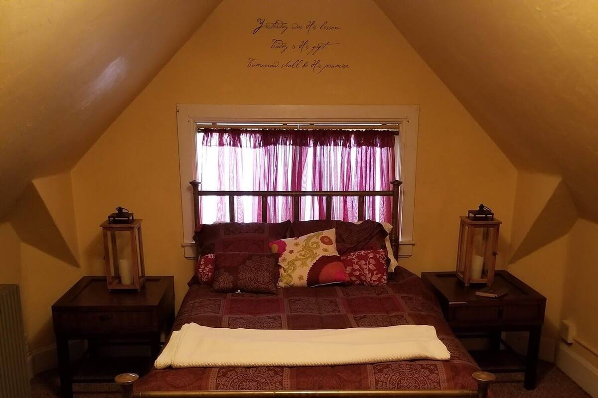 Quarto com uma cama, duas mesas de cabeceira, uma janela com cortinas e uma mesa lateral com abajur.
