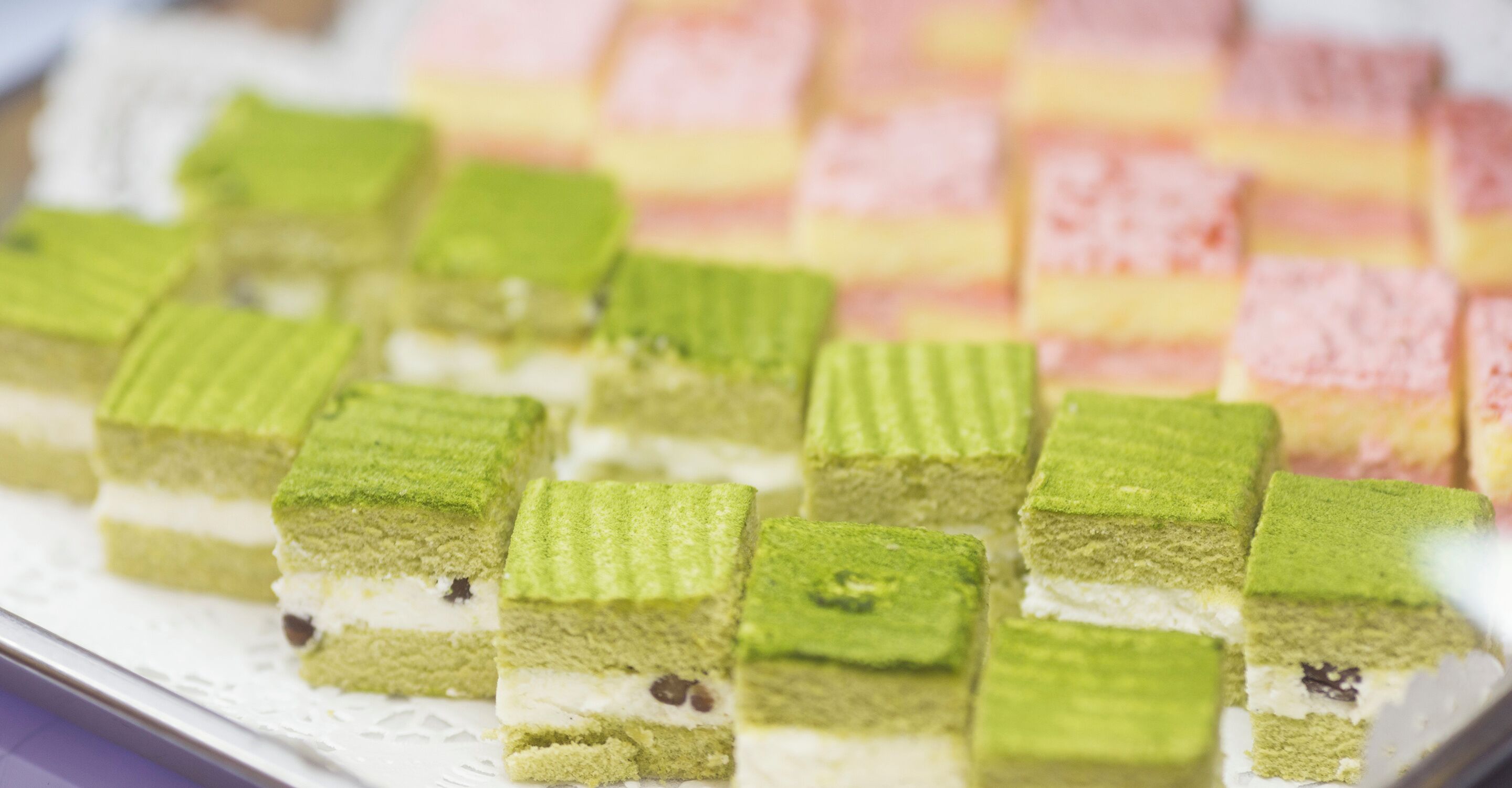 Uma bandeja com sobremesas quadradas, cobertas por uma camada verde, dispostas em um prato branco.