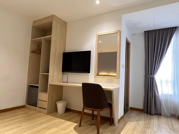 Quarto de hotel moderno com escrivaninha de madeira, televisão de tela plana, espelho e guarda-roupa.