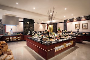 Buffet com diversos tipos de comida, um cozinheiro ao fundo e um design de interiores moderno.