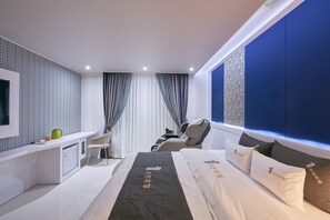 Quarto de hotel moderno com cama, escrivaninha e cadeira de massagem.