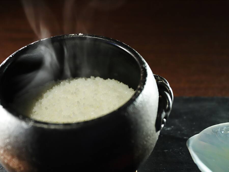 Uma tigela de cerâmica preta cheia de arroz branco sobre uma superfície escura.