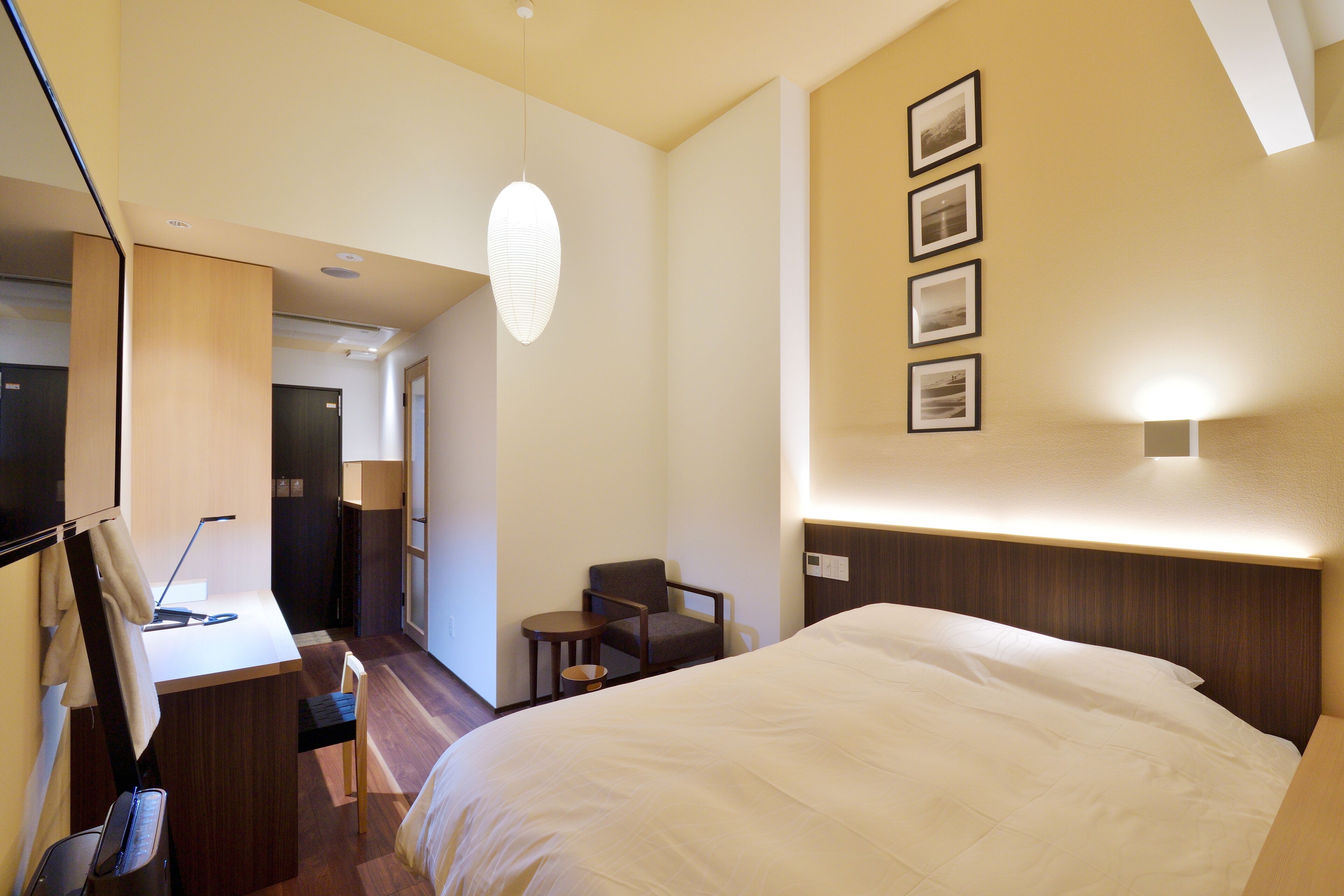 Quarto de hotel com cama, escrivaninha, cadeira e uma mesa pequena.