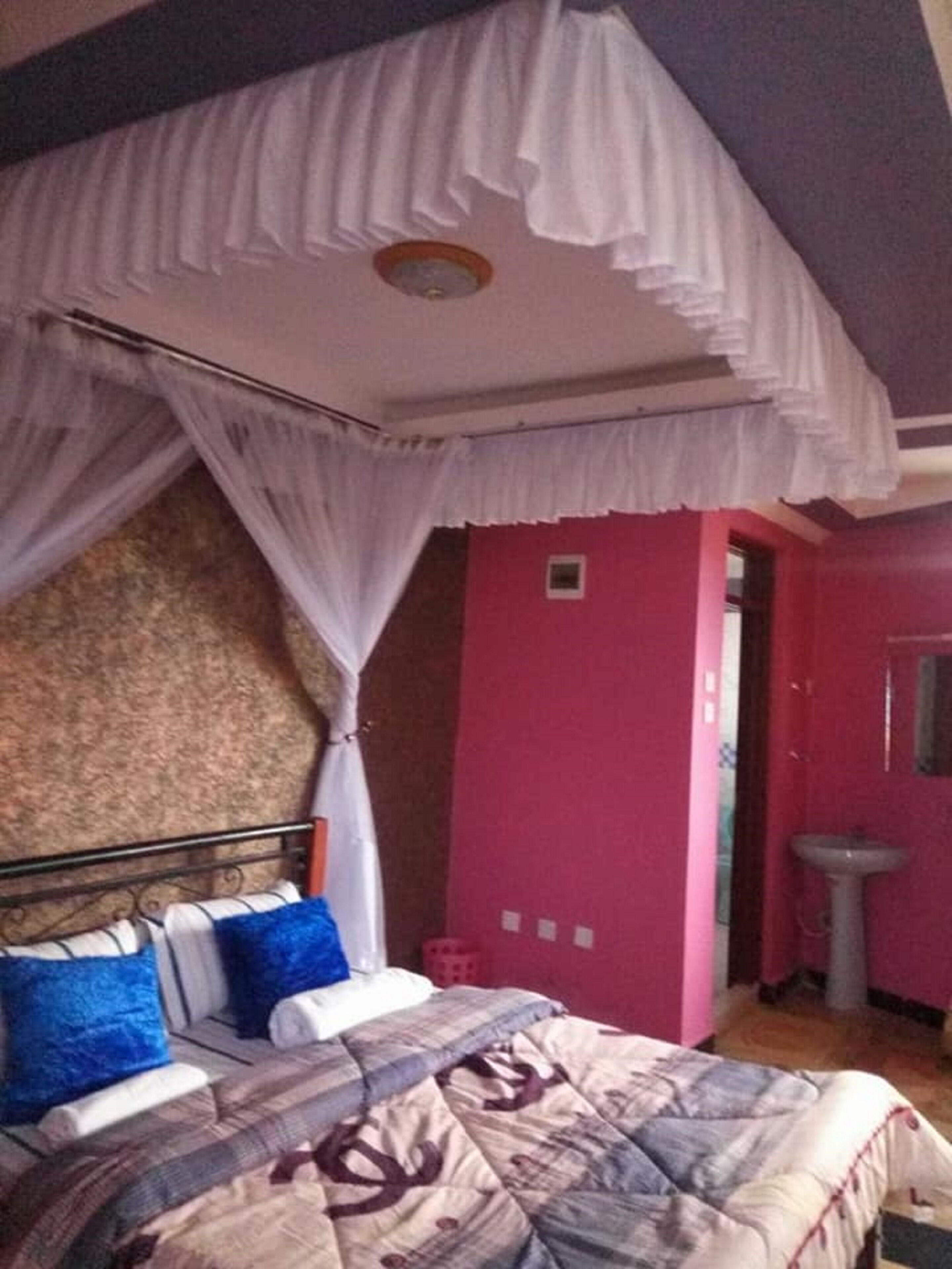 Um quarto com cama, mesa de cabeceira, espelho e parede rosa.