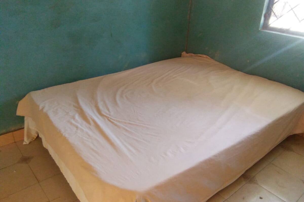 Quarto pequeno e simples, com uma cama, paredes lisas e uma janela.