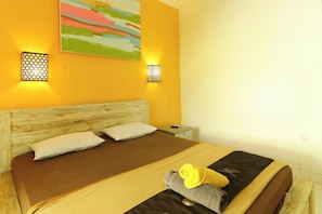Cama com duas almofadas, cabeceira de madeira e mesa de cabeceira com abajur.