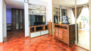Sala de estar com unidade de entretenimento de madeira, uma televisão de tela plana grande e objetos decorativos nas prateleiras.