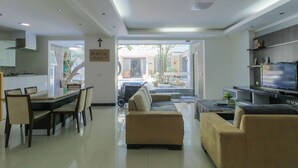 Uma sala de estar moderna com área de jantar, sofá, TV e vista para o exterior.