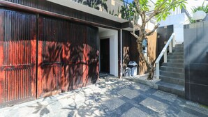 Edifício moderno com uma grande porta de madeira para garagem, uma escadaria e uma árvore em primeiro plano.