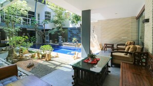 Um jardim interno moderno com piscina, mobiliário de madeira e diversas plantas.
