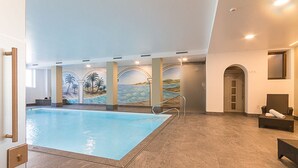 Piscina com um mural de palmeiras e colinas, área de spa com uma cadeira e uma porta com a inscrição 'SPA'.
