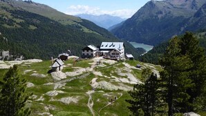 Uma pousada de montanha com um edifício grande e construções menores, cercada por colinas verdejantes e um lago.