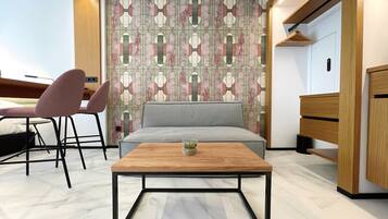 Uma sala de estar moderna com um sofá cinzento, duas cadeiras cor-de-rosa, uma mesa de centro de madeira e um papel de parede estampado.
