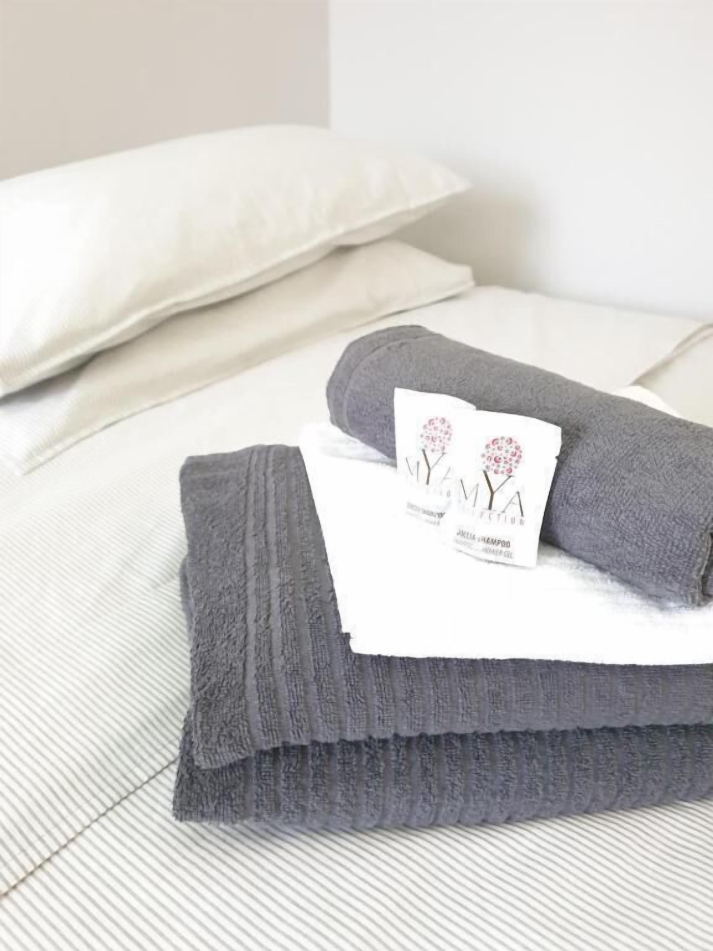 Uma cama bem arrumada com uma toalha cinza dobrada e um travesseiro branco.