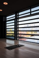 Um quarto espaçoso com janelas amplas, piso de madeira e um tapete de yoga com halteres.