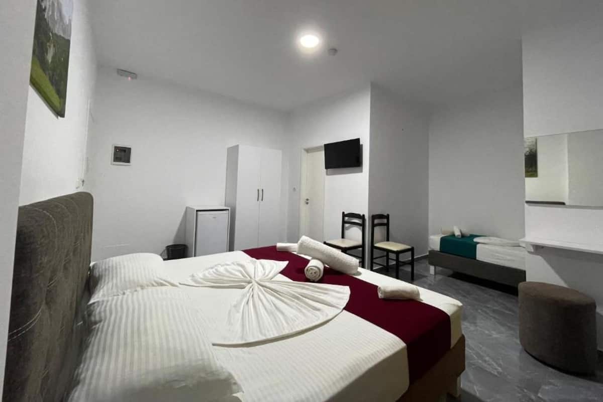Quarto de hotel com cama, escrivaninha, cadeira, armário e televisão.