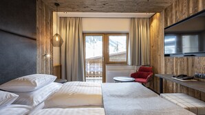 Quarto de hotel com cama, uma cadeira vermelha, uma mesinha, televisão e janela com vista para as montanhas.