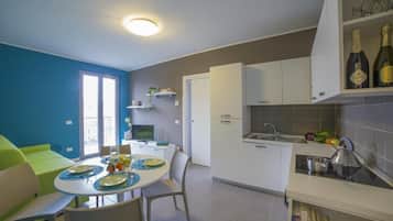 Uma cozinha moderna com armários brancos, um espaço de jantar com mesa posta para dois e uma parede azul vibrante.
