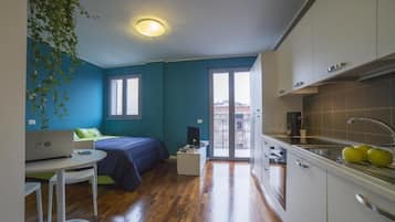 Quarto compacto com cama, uma pequena mesa, um laptop, pia e janela.