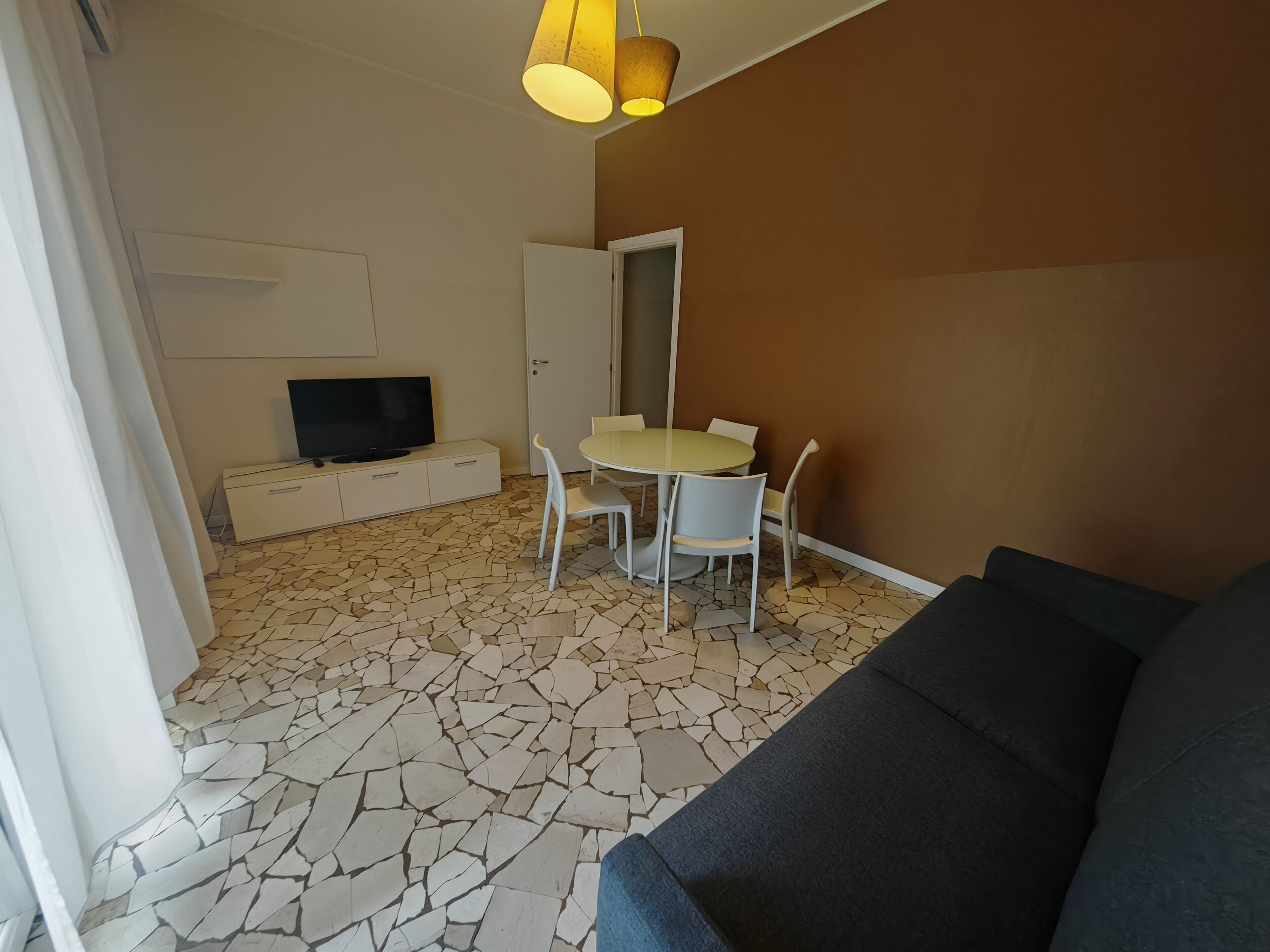 Sala de estar com sofá, televisão, mesa de jantar e cadeiras, e piso estampado.