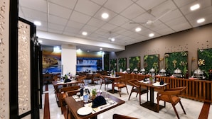 Restaurante com várias mesas e cadeiras, um ventilador de teto e painéis decorativos na parede.
