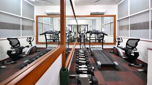 Uma academia com equipamentos de ginástica, espelhos e um ventilador de teto.