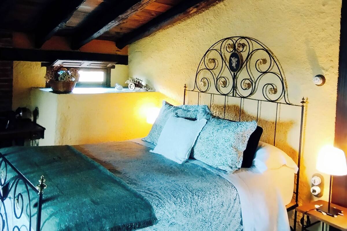 Quarto com cama, mesa de cabeceira, luminária, janela e teto de madeira.