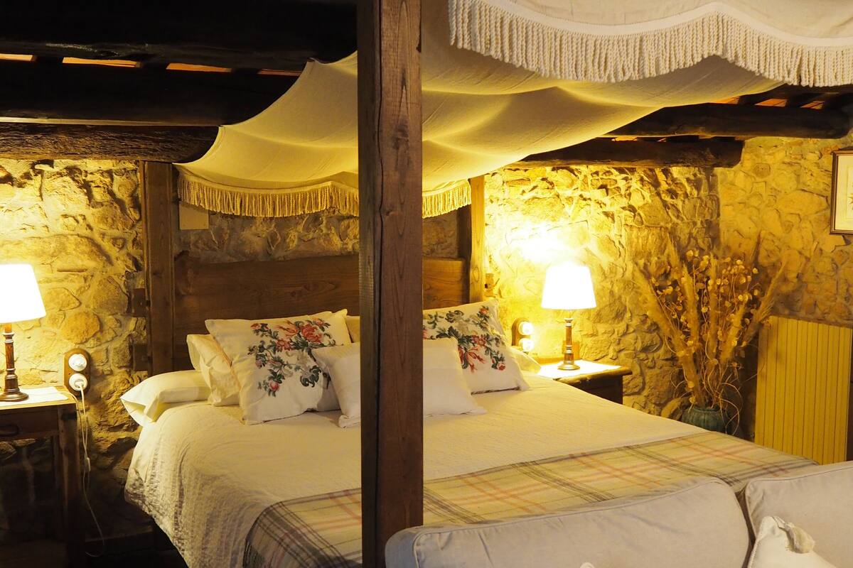 Um quarto rústico com cama de dossel, paredes de pedra e vigas de madeira.