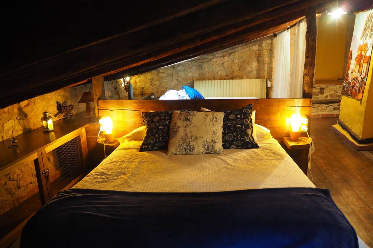 Um quarto aconchegante com parede de pedra, cabeceira de madeira e cama com almofadas estampadas.