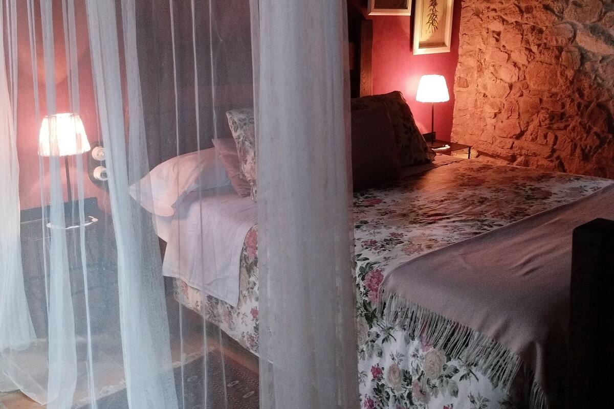 Quarto com cama, mesa de cabeceira, abajur, quadro pendurado na parede e parede de pedra.